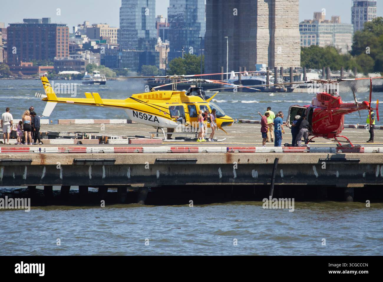 yellow and white helicopter and red helicopter on a helipad with people ...