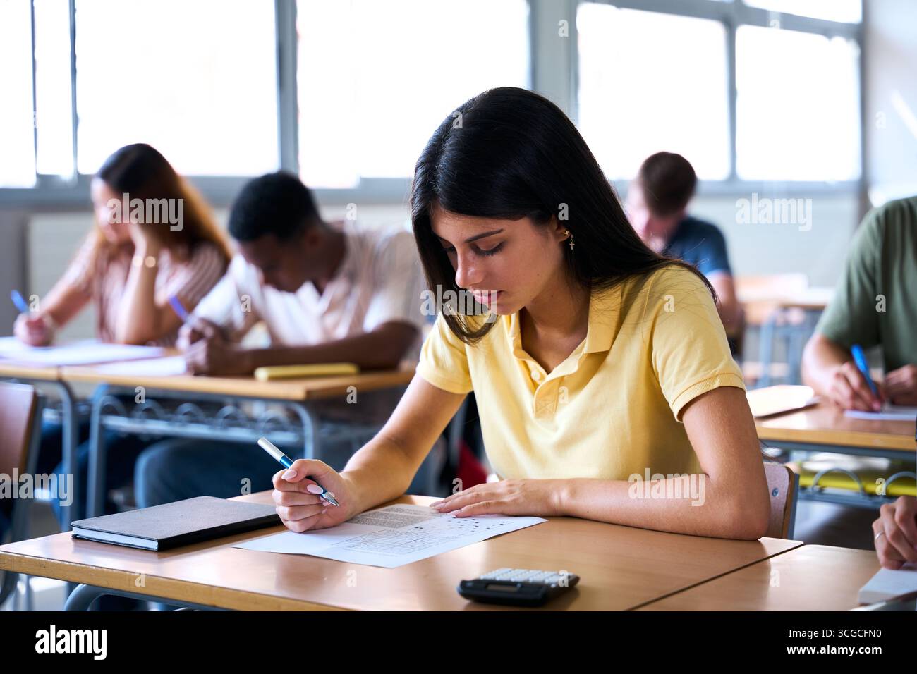 Focused student taking exam in classroom with calculator and notebook ...
