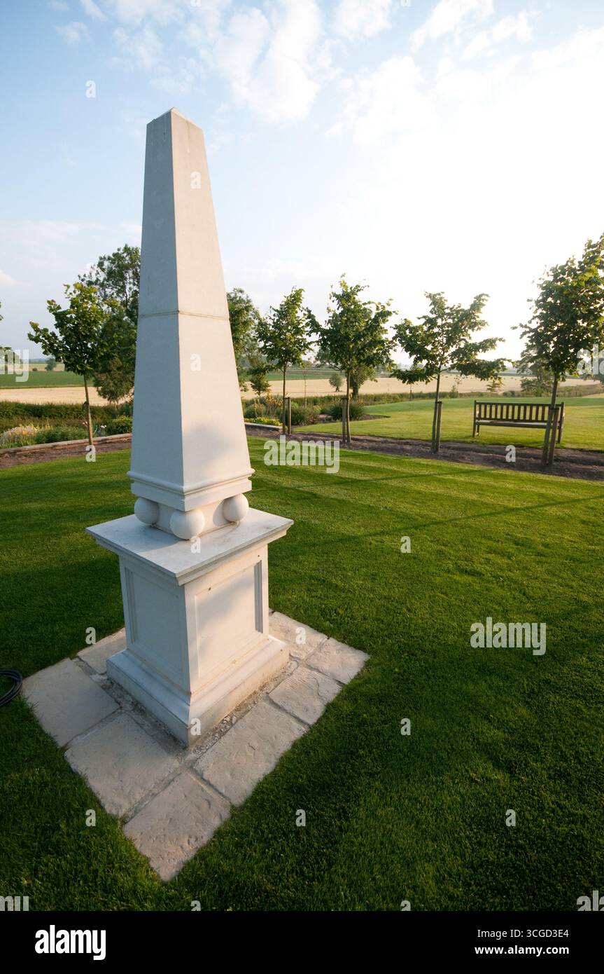 A white obelisk stands prominently in a well-kept garden, surrounded by ...