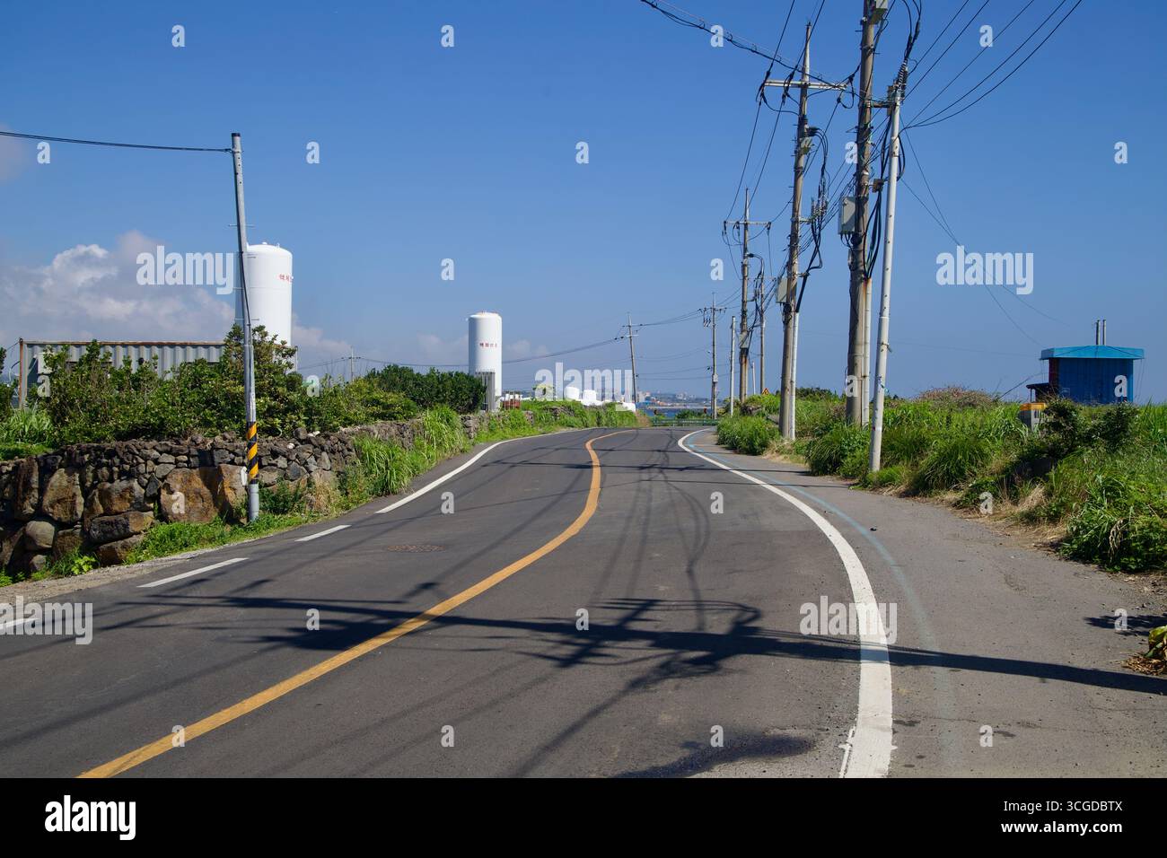 Utility poles and white storage tanks line a narrow two‑lane road near ...