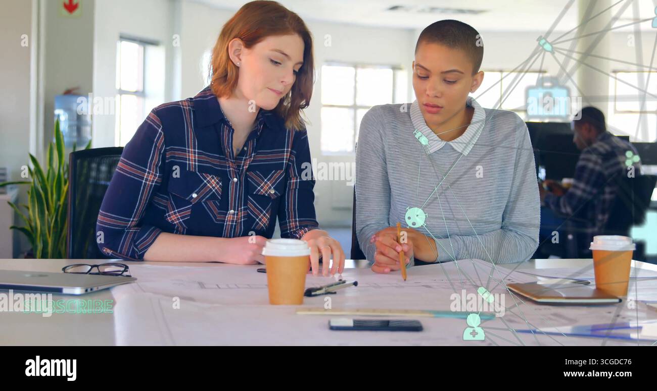 Two women colleagues reviewing large-format plans in office, with ...