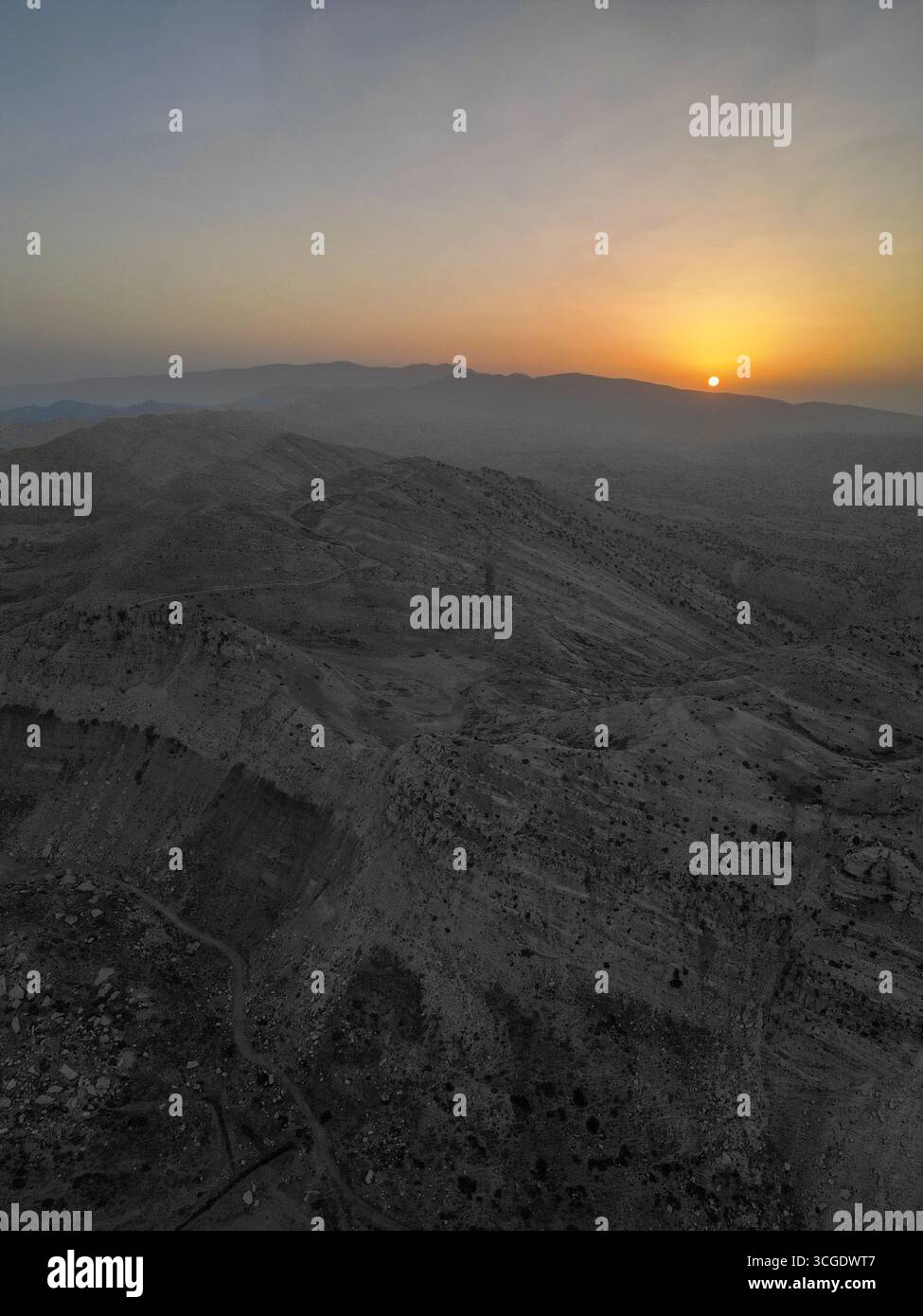 Aerial view of the sun setting over the rugged, mountainous terrain ...