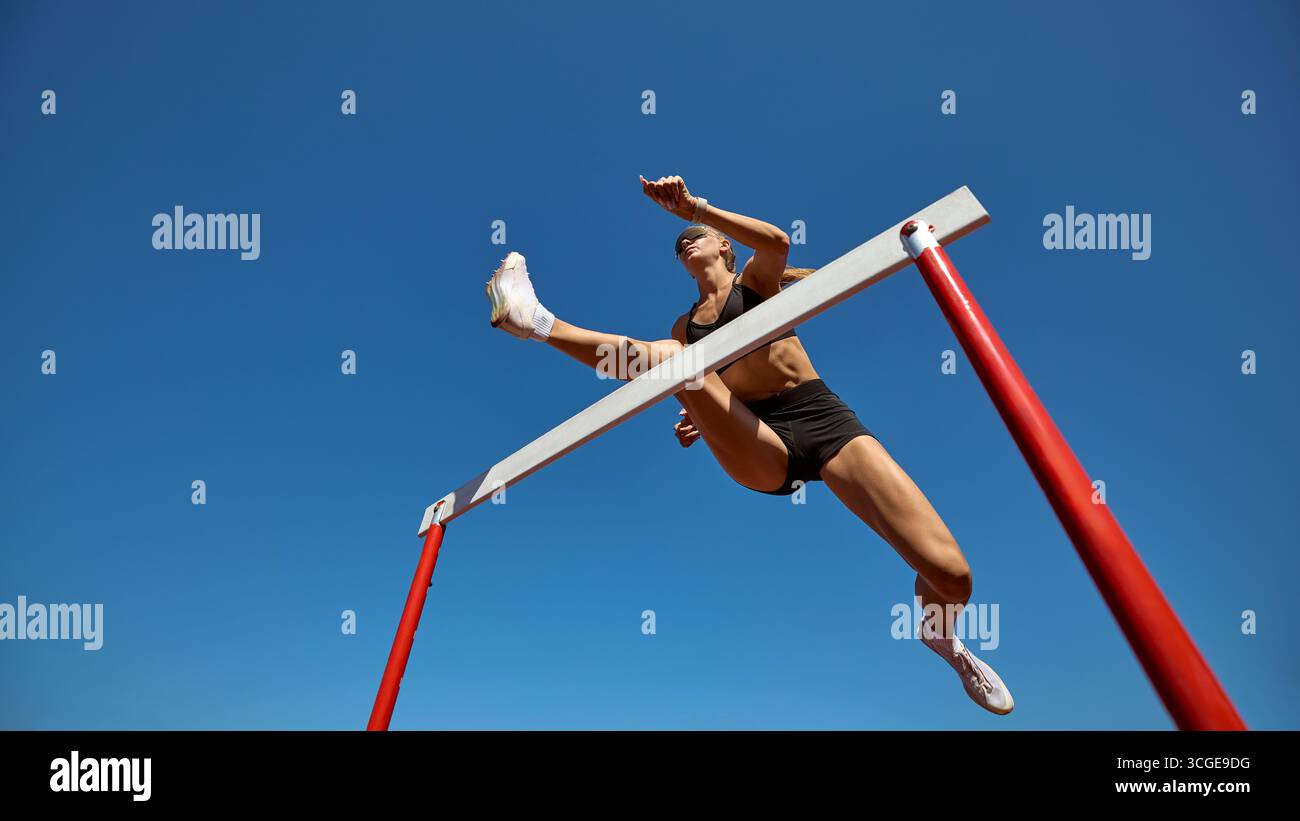 Female hurdler in low angle action leap against clear sky Stock Photo ...
