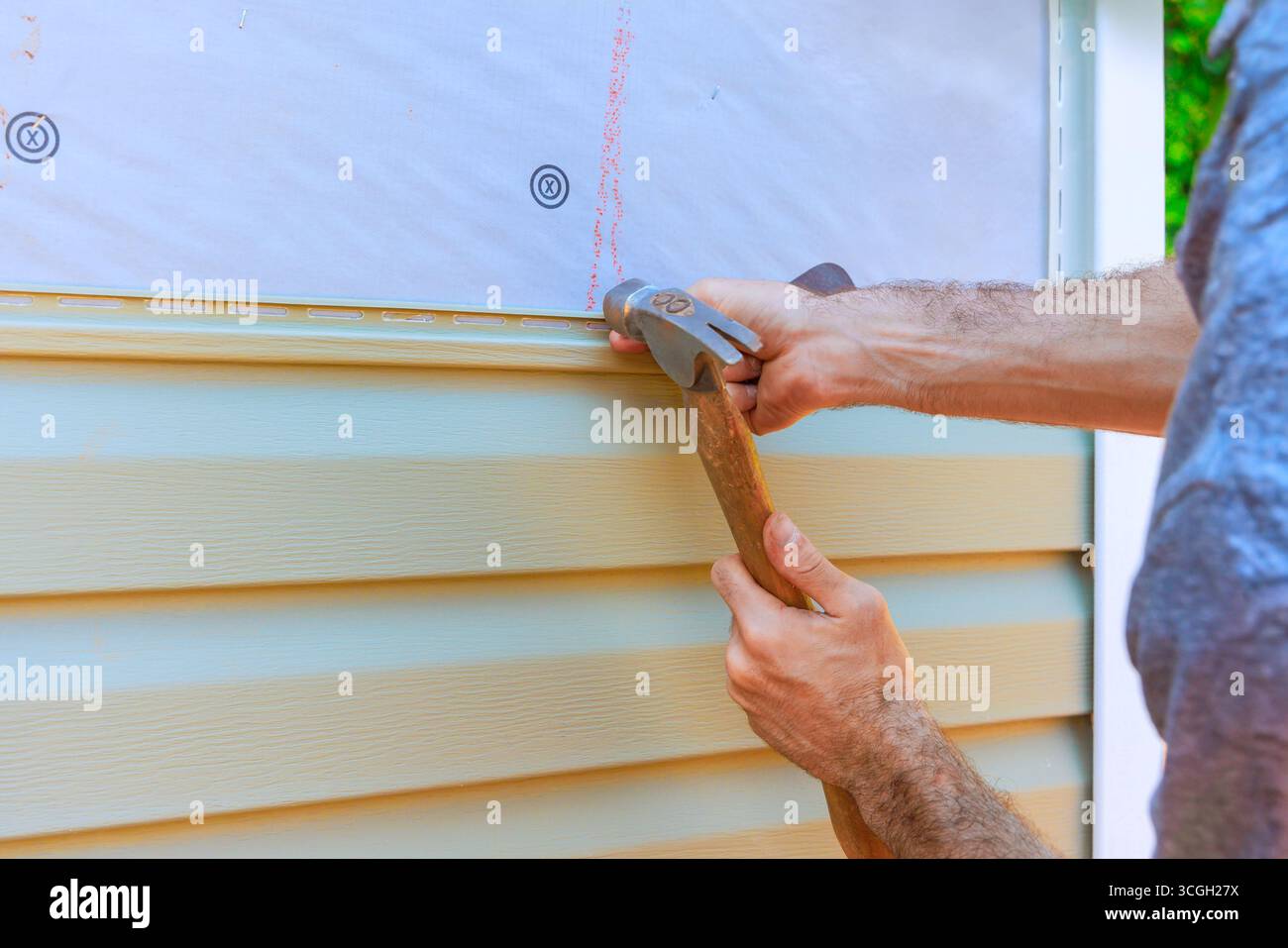Worker is using hammer to secure new PVC vinyl siding while working on ...