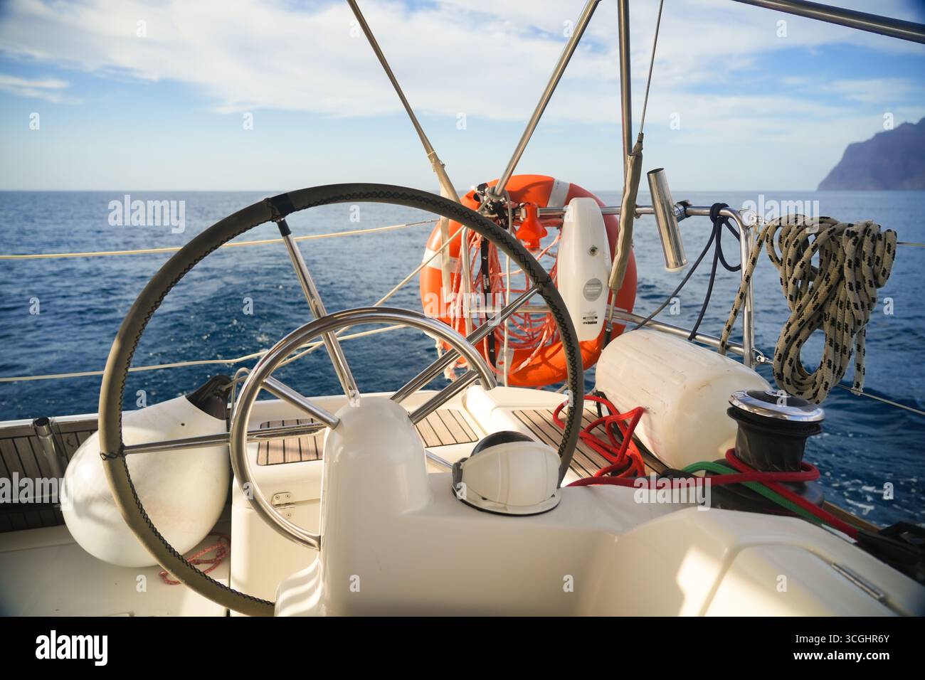 Sailing yacht cockpit with stainless helm, lifebuoy, winch and coiled ...