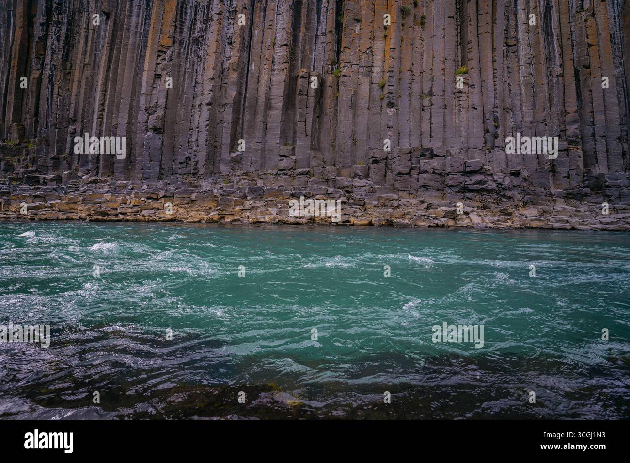 Turquoise glacial waters flow past towering basalt columns in Stuðlagil ...