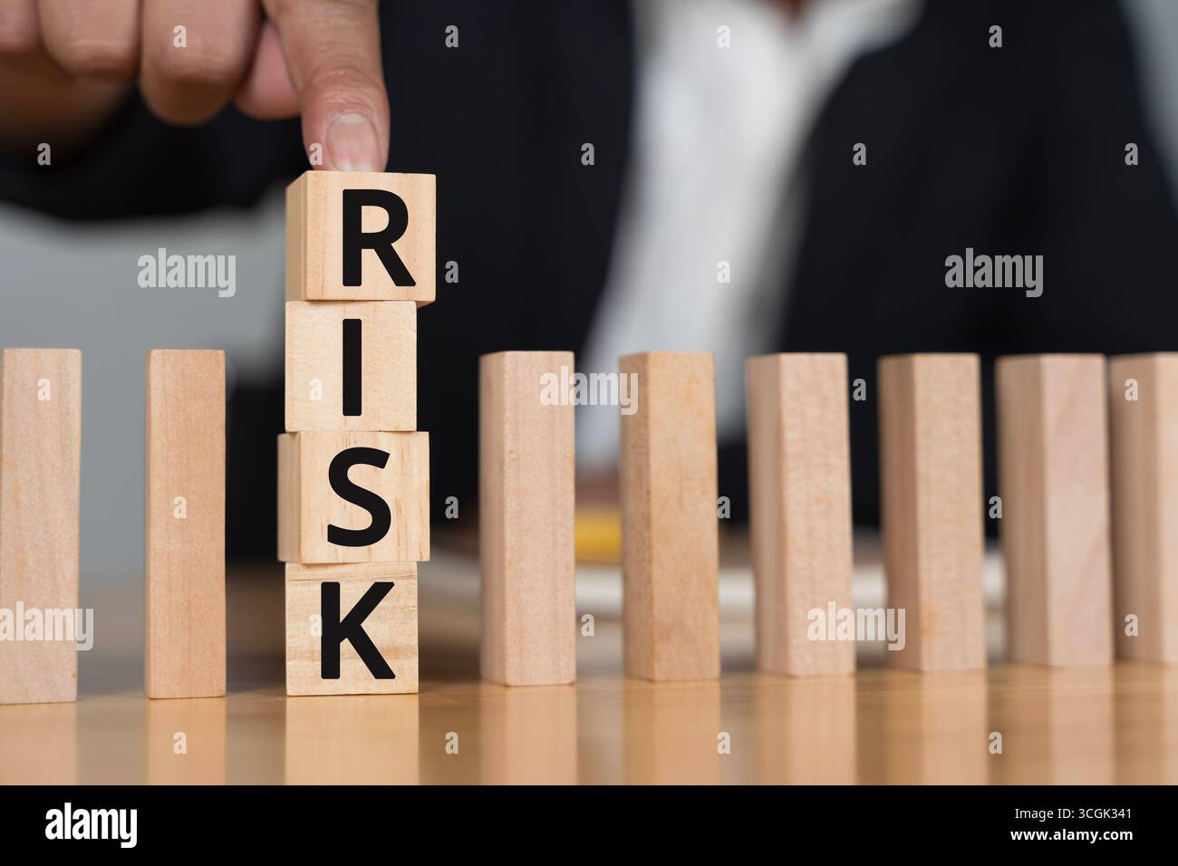 Close-up hand placing wooden blocks spelling risk among domino pieces ...