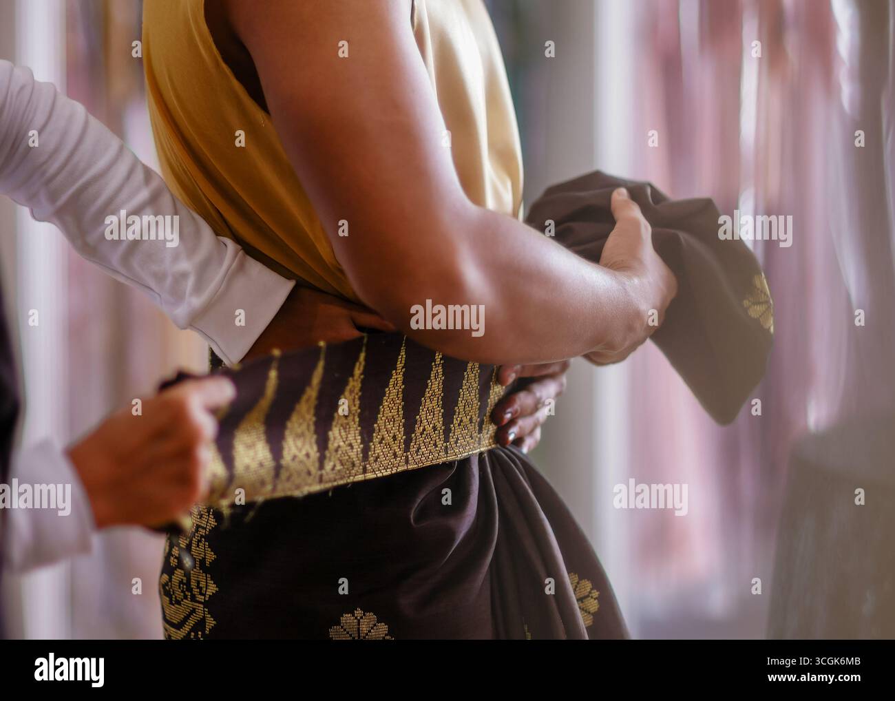 Close-up of hands adjusting a traditional Malay songket waist wrap or ...