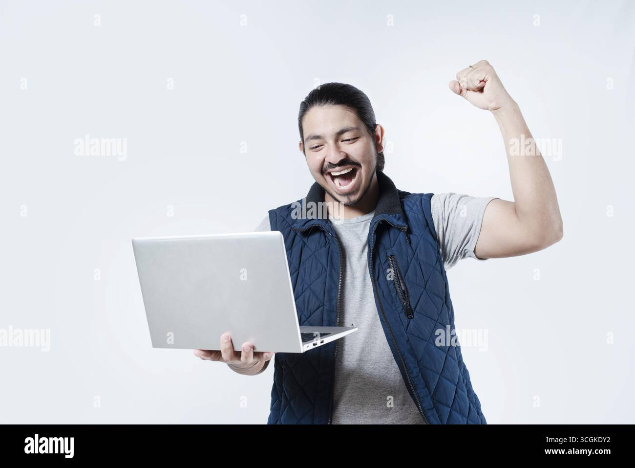 Young man celebrating holding a computer on isolated background. Male ...