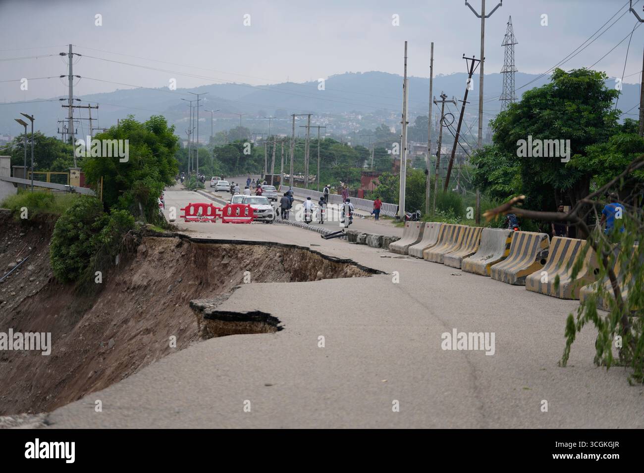 Commuters pass by a washed out road in the aftermath of flash floods ...
