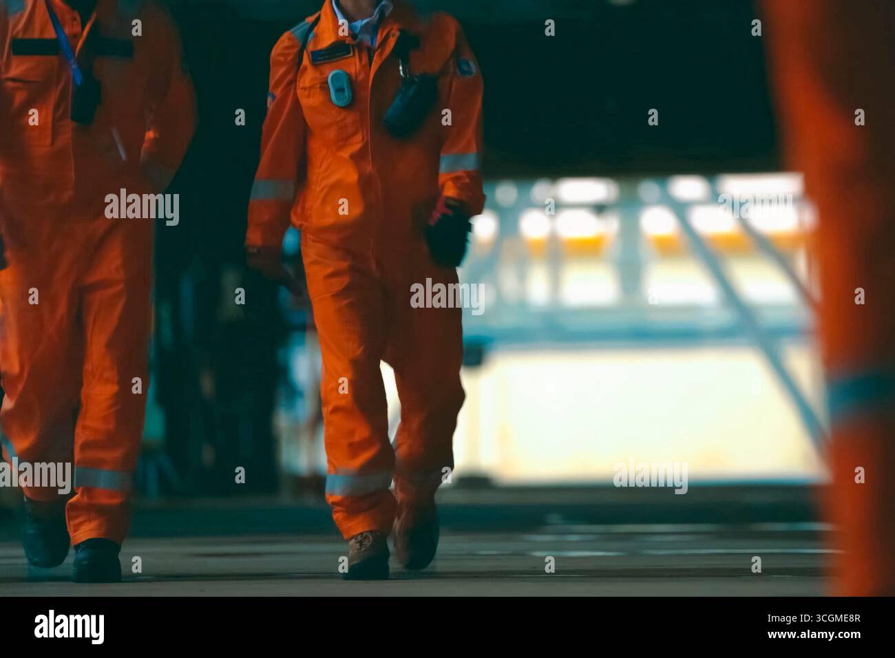 A group of oil rig workers in orange overalls going to a work shift ...