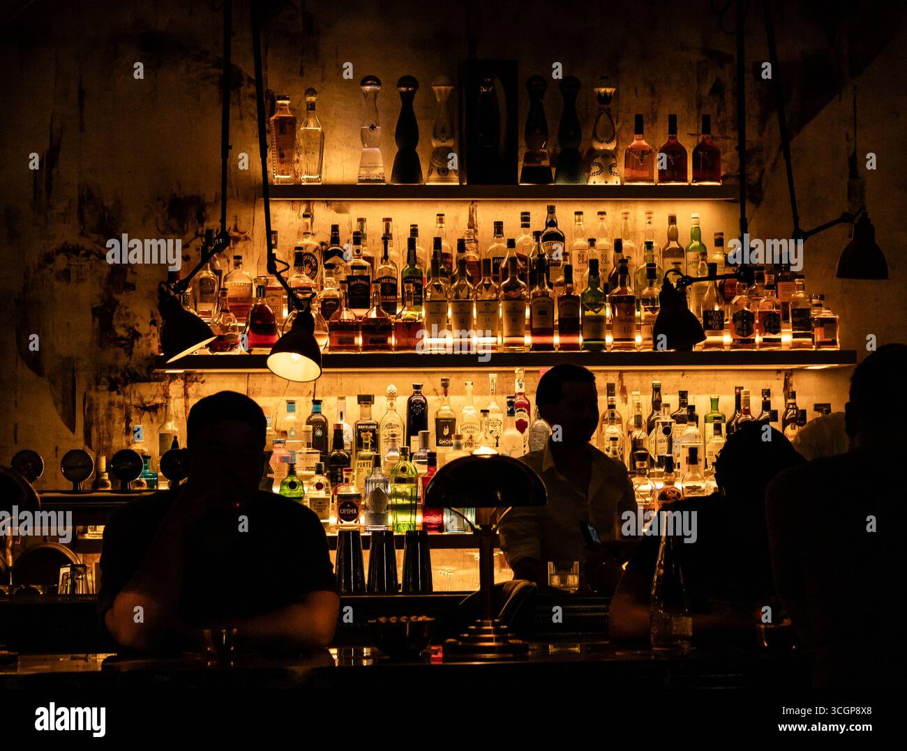 A cozy, atmospheric bar featuring shelves of illuminated liquor bottles ...