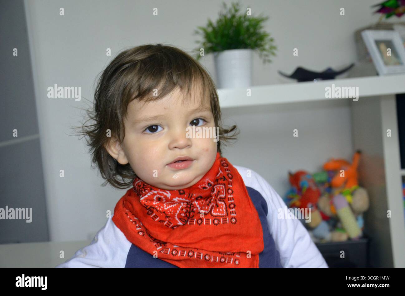 A cheerful two-year-old boy eat while looking directly into the camera ...