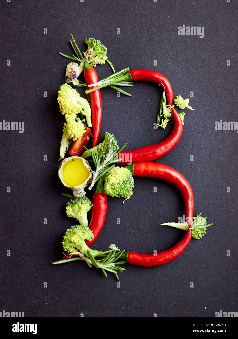 Creative letter B arranged from chili peppers, broccoli, rosemary ...
