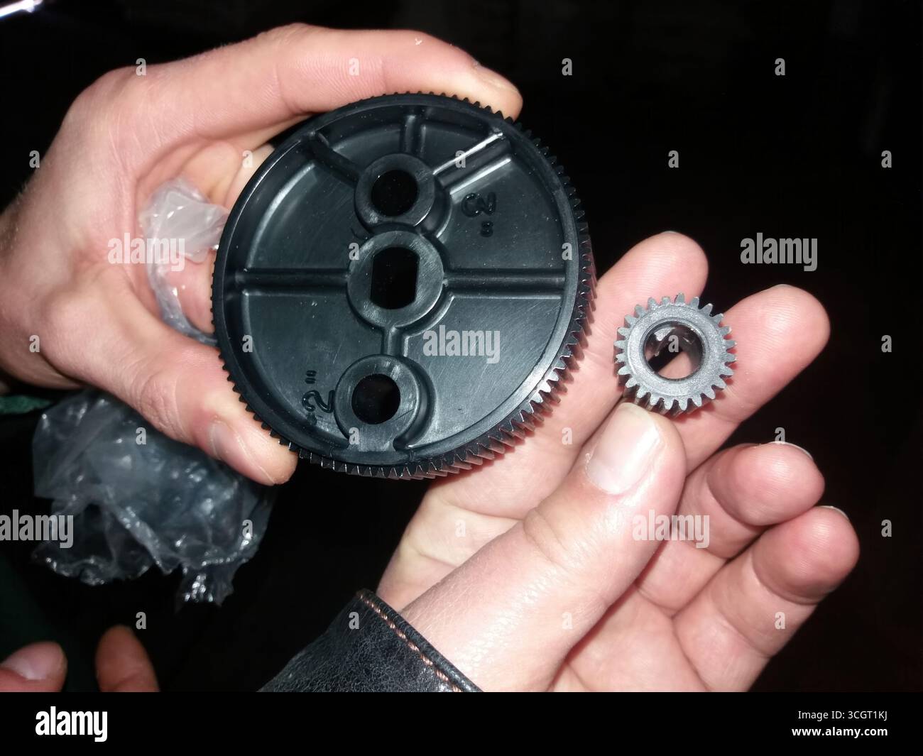 Detailed view of hands holding two plastic gears, including a larger ...