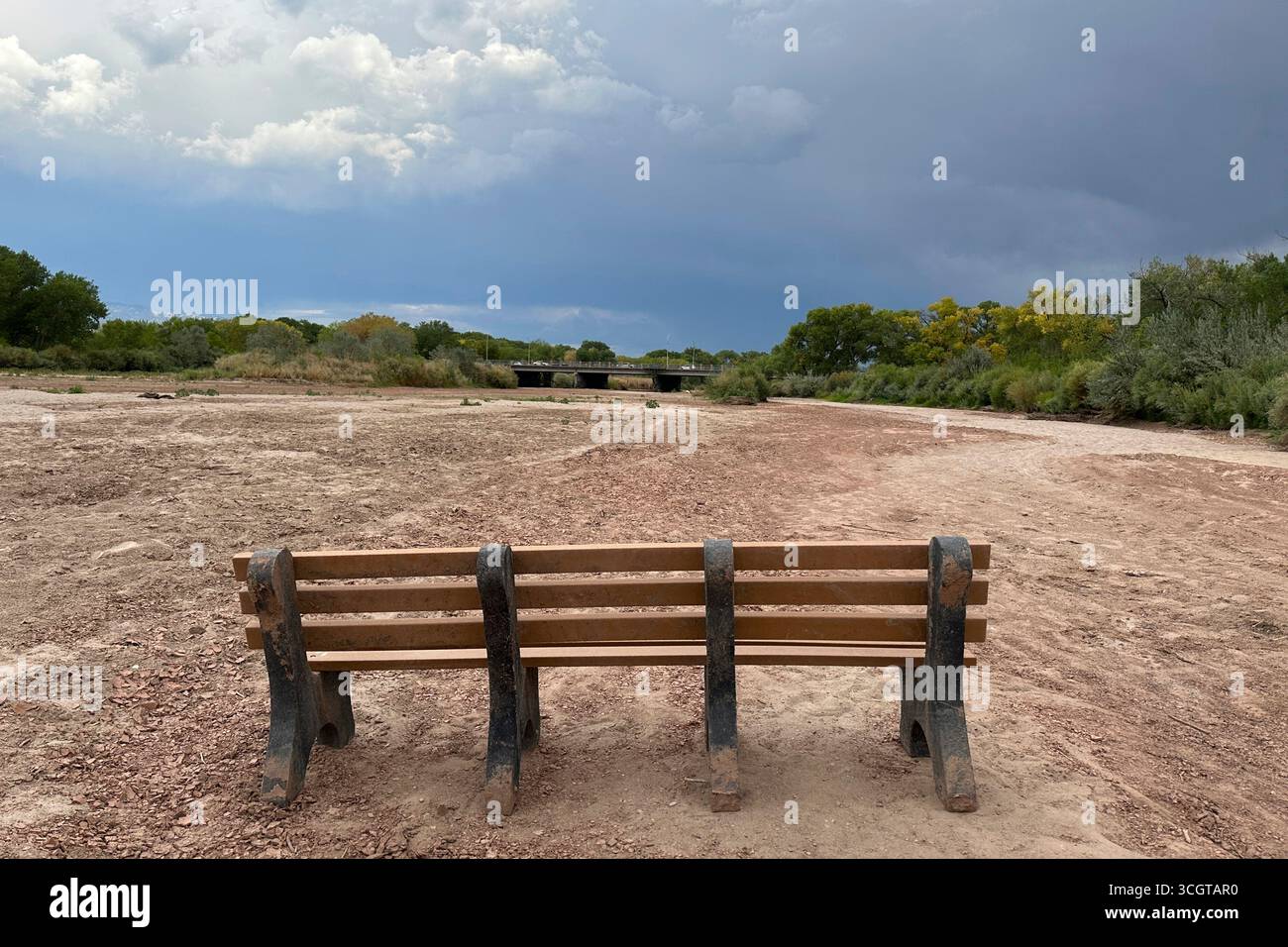 A park bench sits in the dry riverbed of the Rio Grande as traffic ...
