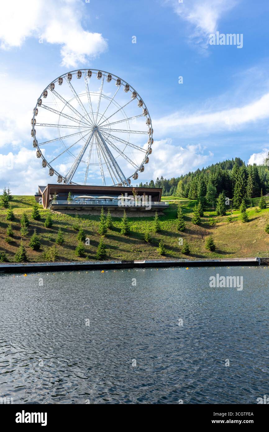 Ferris wheel by the water with pine slopes around. Lake and ride Stock ...