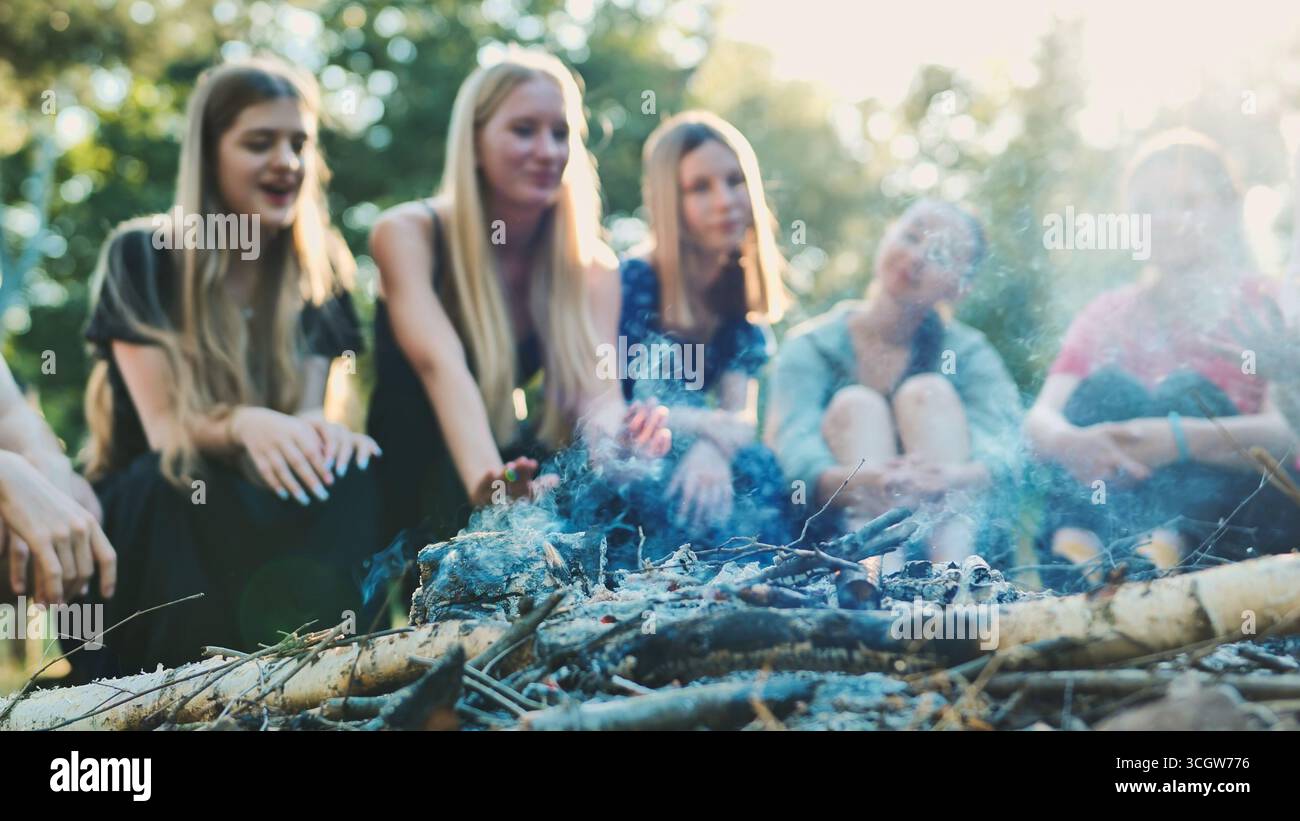 School friends warming up around a bonfire in summer camp, enjoying ...