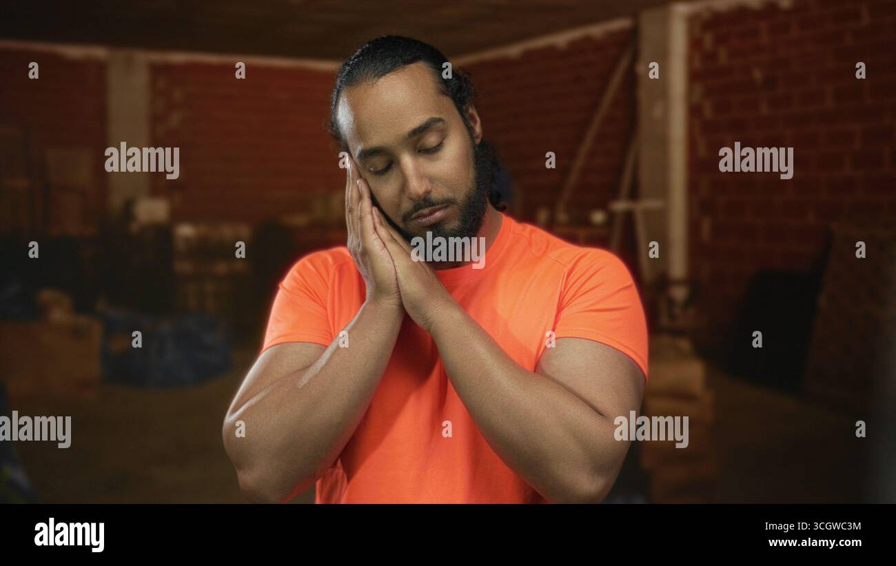 Man wearing bright orange shirt with hands pressed to cheek inside ...