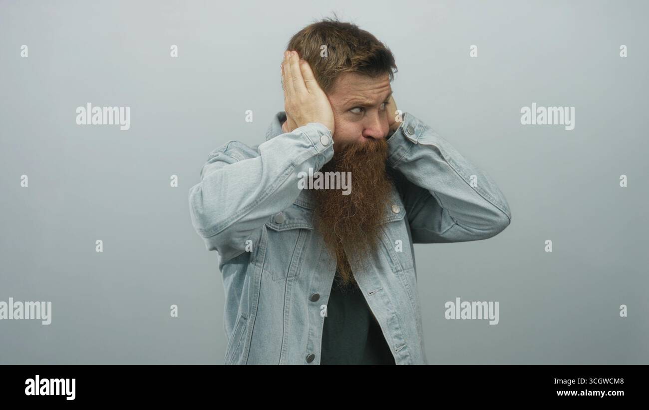 Young caucasian bearded man tightly covers ears with both hands and ...
