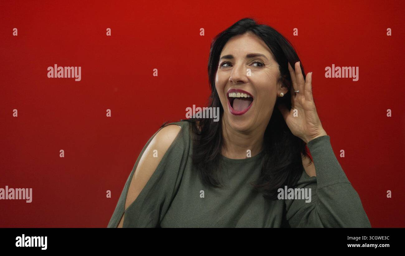 Woman cupping her right ear and leaning forward in studio with bright ...