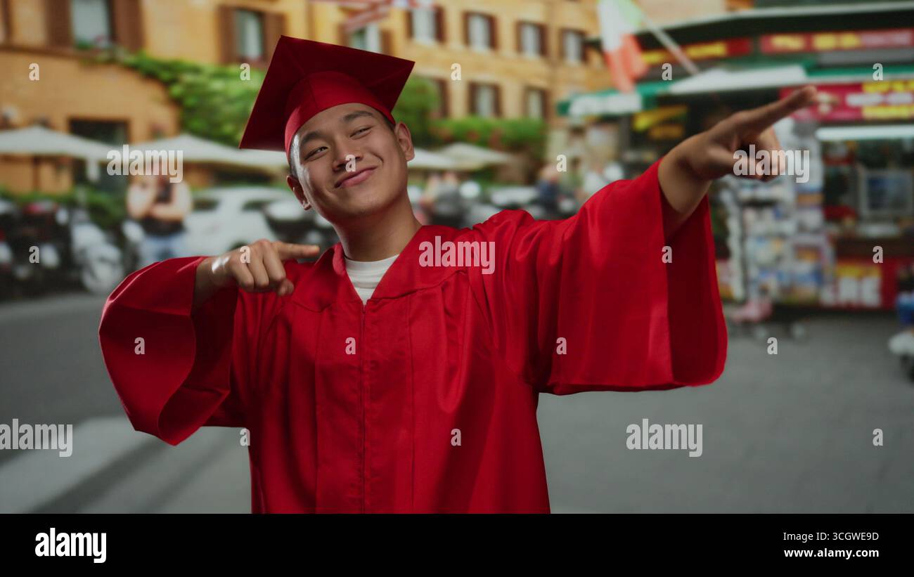 Young man in red graduation gown and mortarboard points and smiles ...