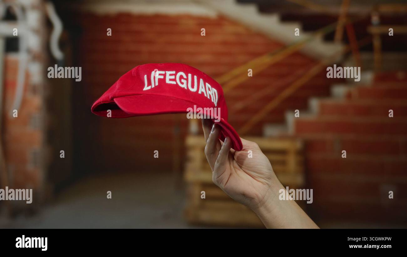 Hand holding red lifeguard hat in indoor construction site with bricks ...
