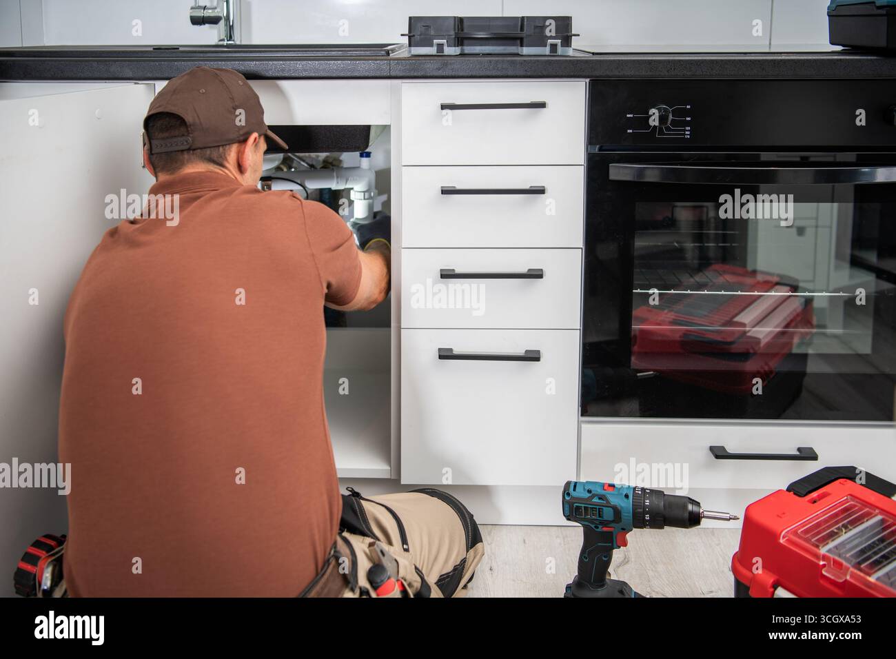 A technician is working underneath a kitchen sink, installing equipment ...