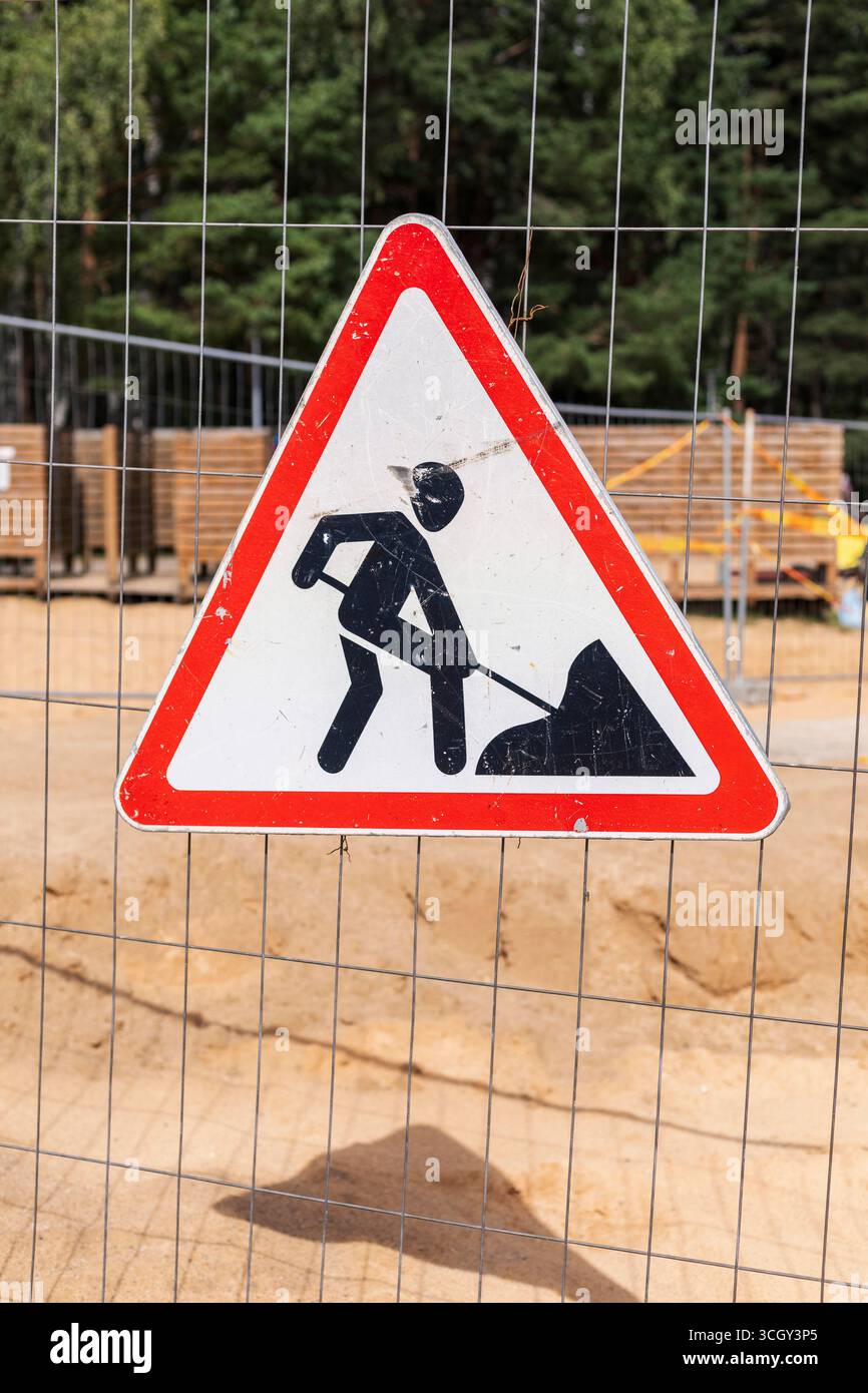 A triangular warning sign displaying a construction worker digging. The ...