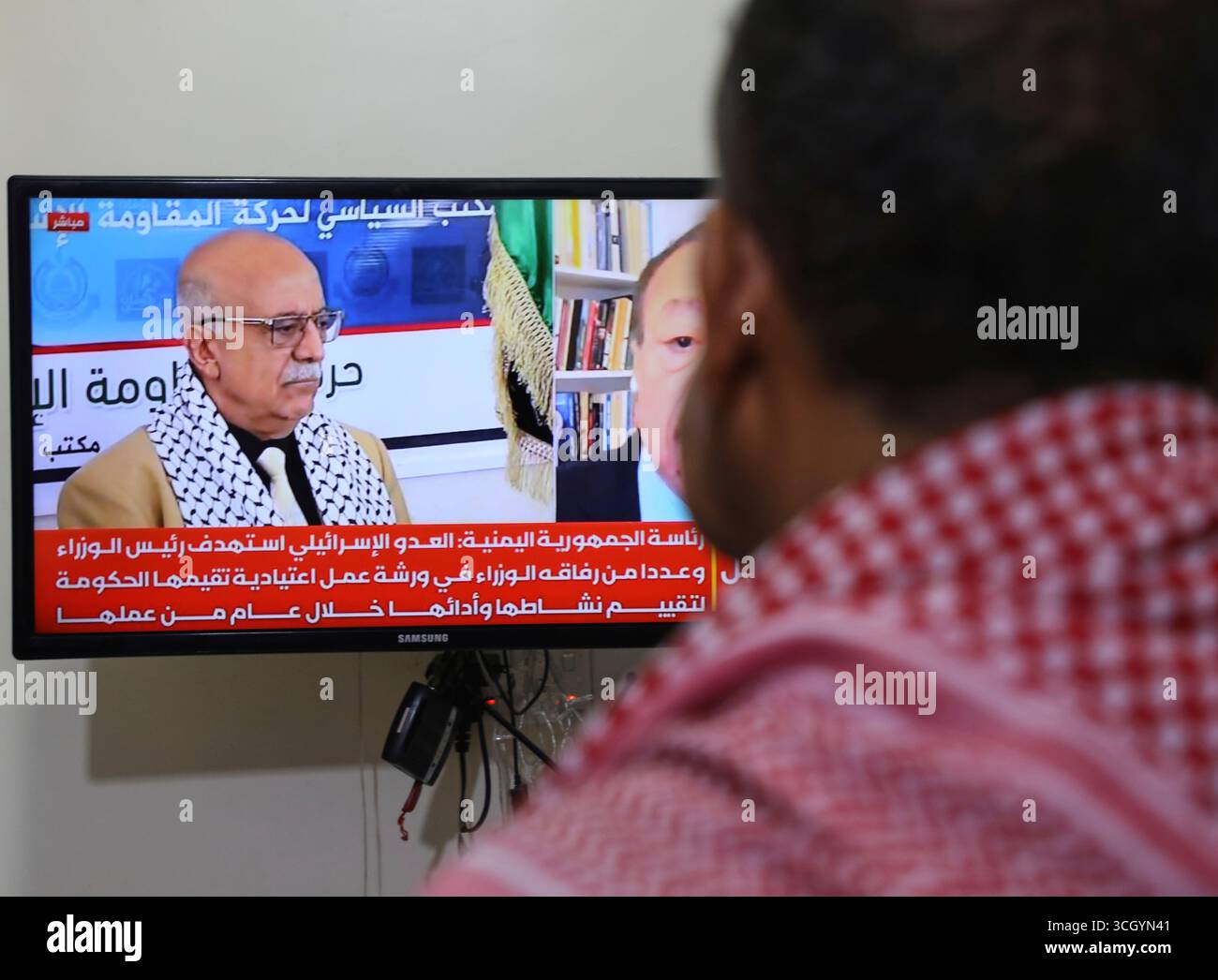 A man watches the news on TV, displaying footage of Ahmed al-Rahawi ...