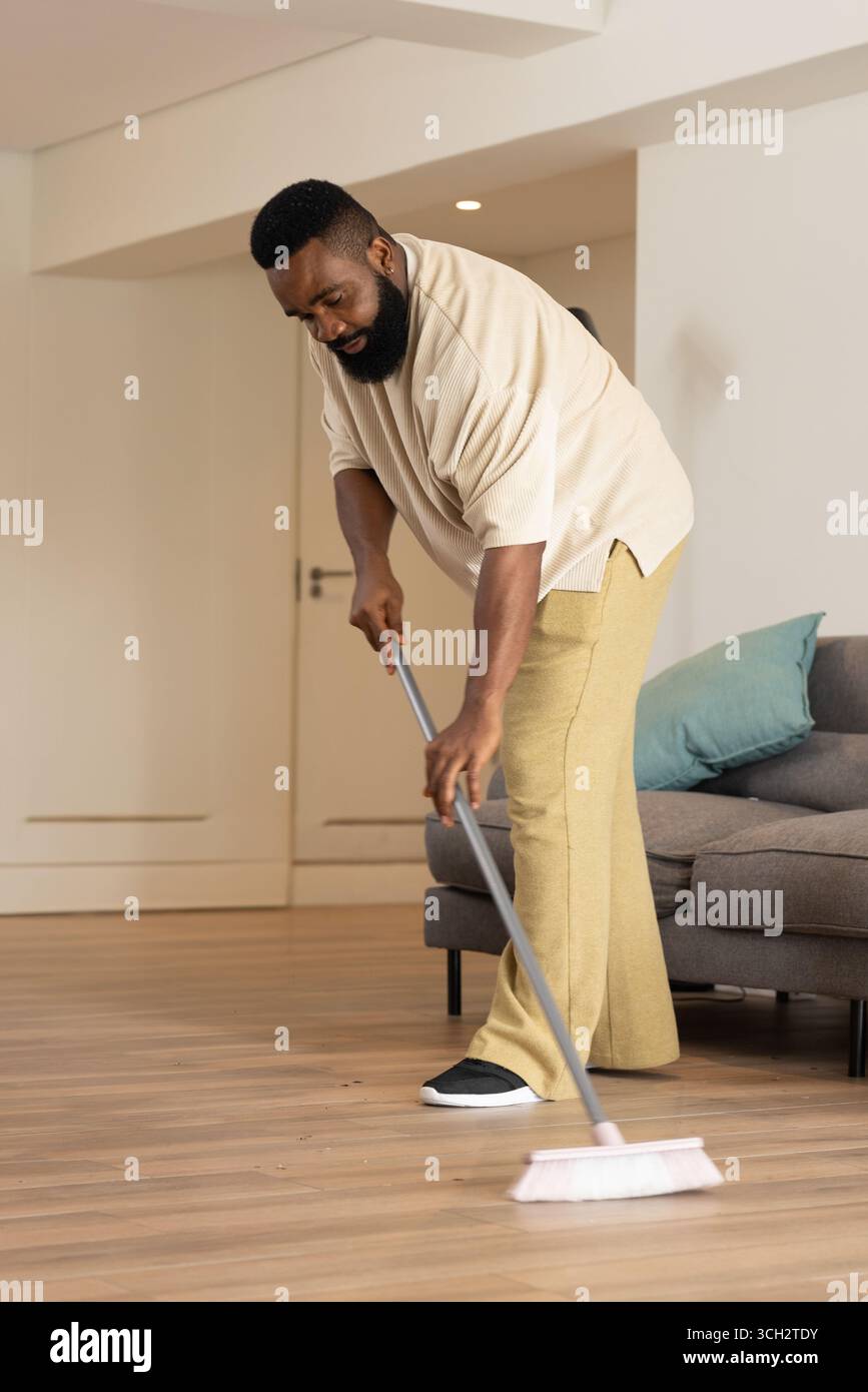 African American man sweeping light hardwood floor with push broom in ...