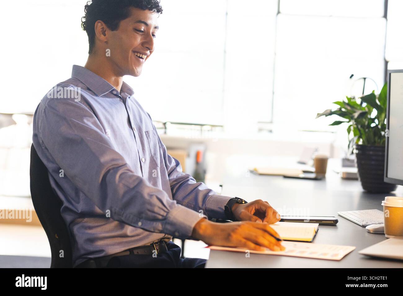 Man reviewing documents at office desk in front of large windows, with ...