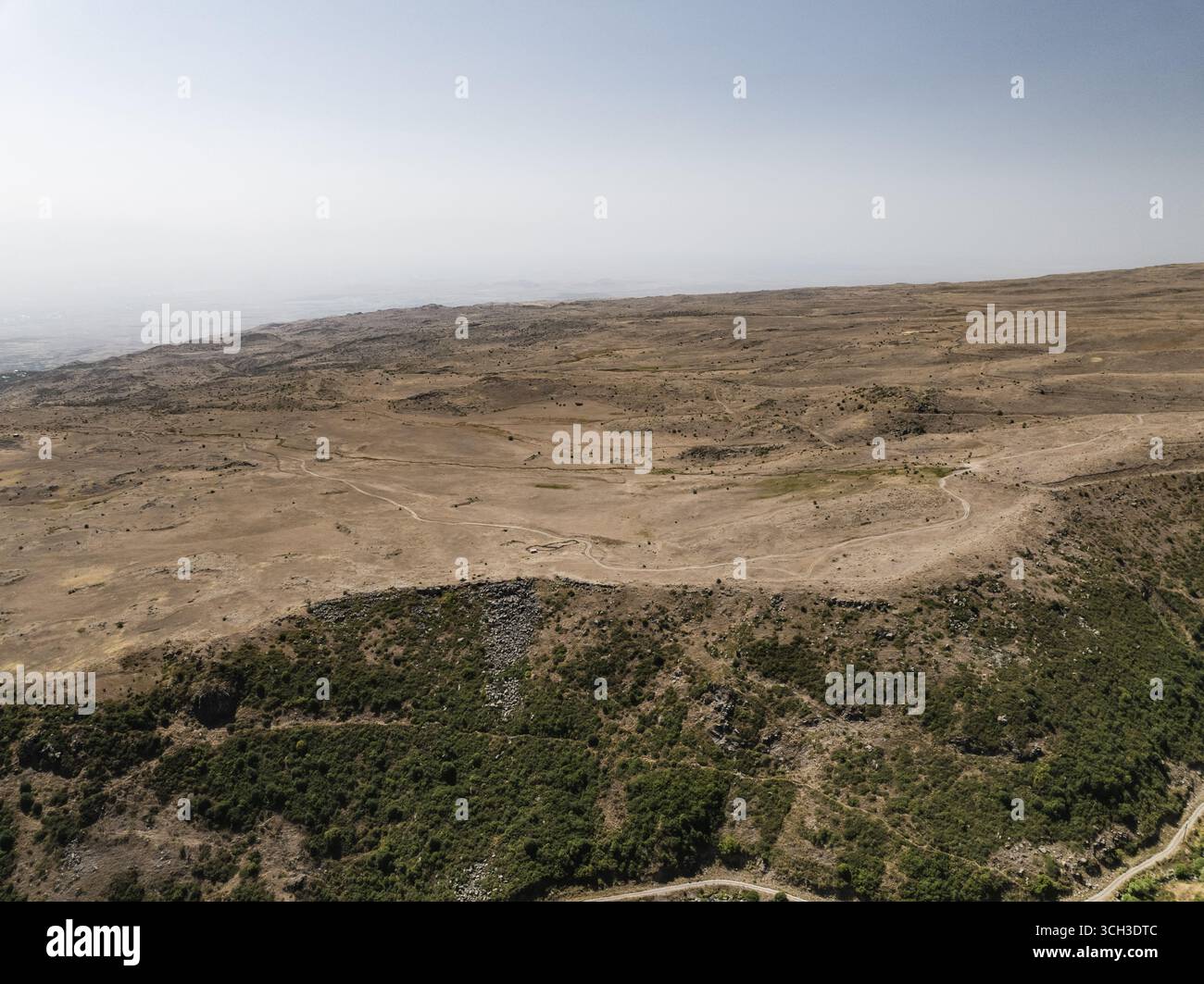 Aerial view of arid highlands meeting lush forests under a hazy sky, a ...