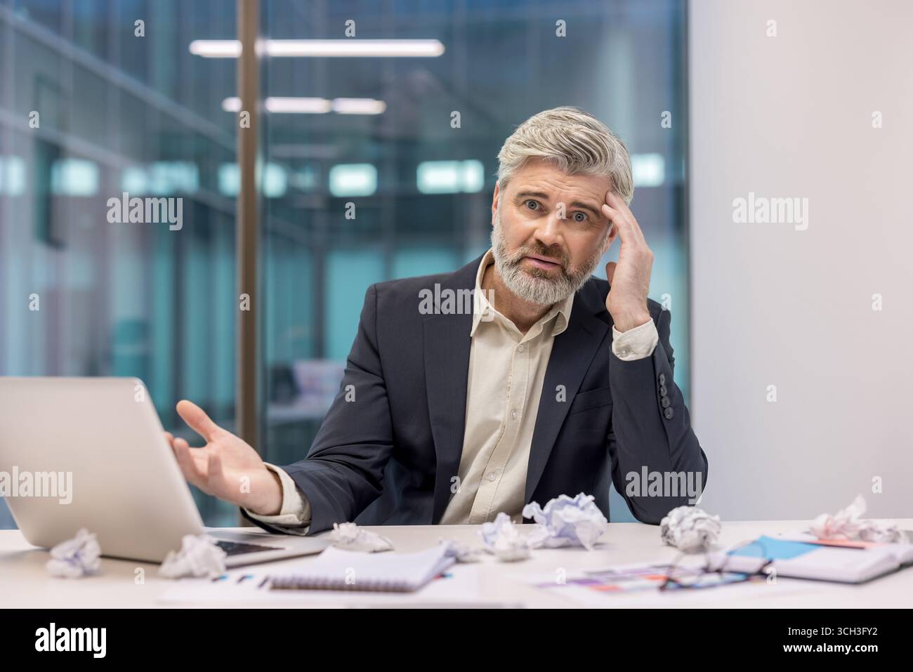 A frustrated businessman seated at his desk in a modern office setting ...