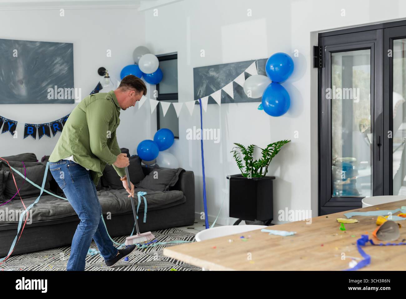 middle-aged man sweeping floor with broom in living room, clearing ...