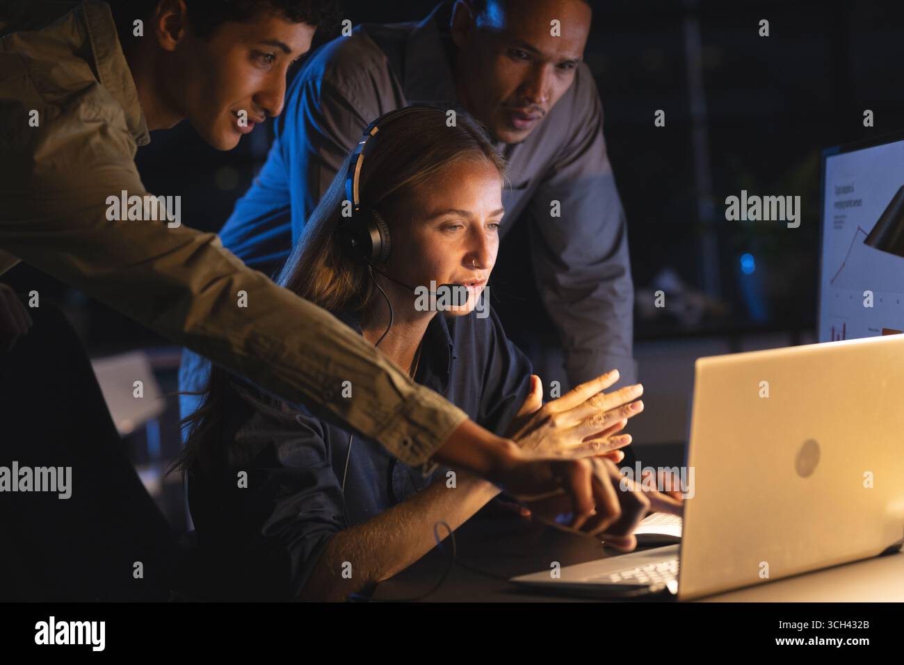 Team collaborating at night, focused on laptop screen, discussing ...