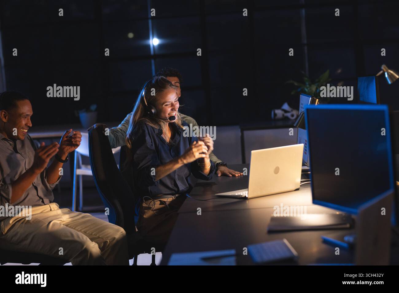 Team celebrating success at office, using laptops and headsets during ...