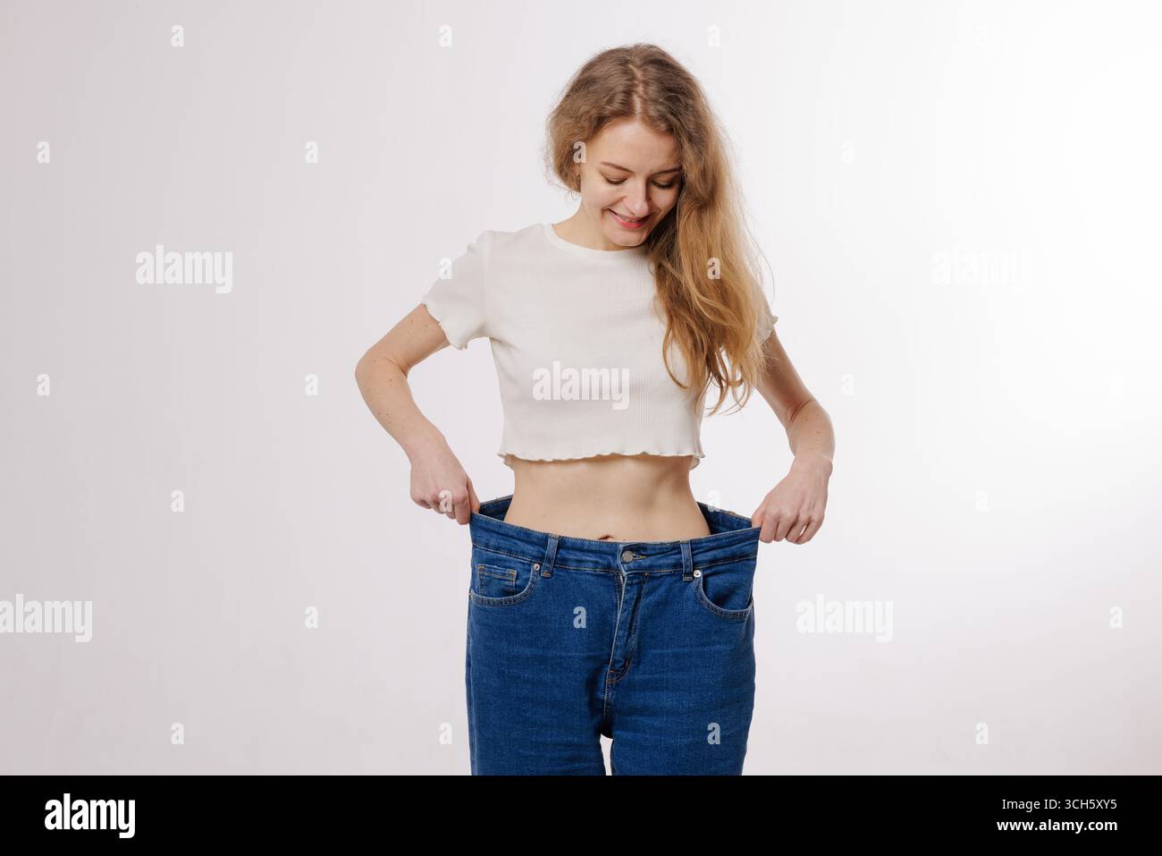 Slim woman smiling in loose jeans, celebrating successful weight loss ...