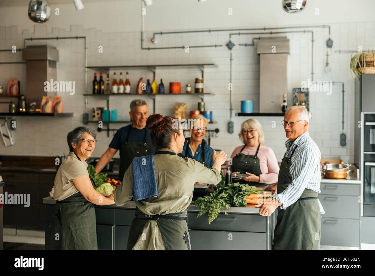 Rear view of female chef teaching senior students in cooking class at ...