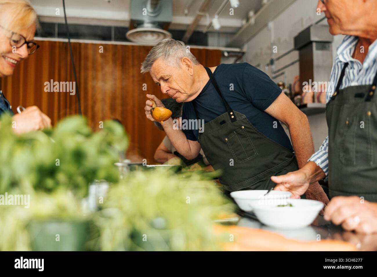 Senior man smelling food while learning in cooking class with friends ...