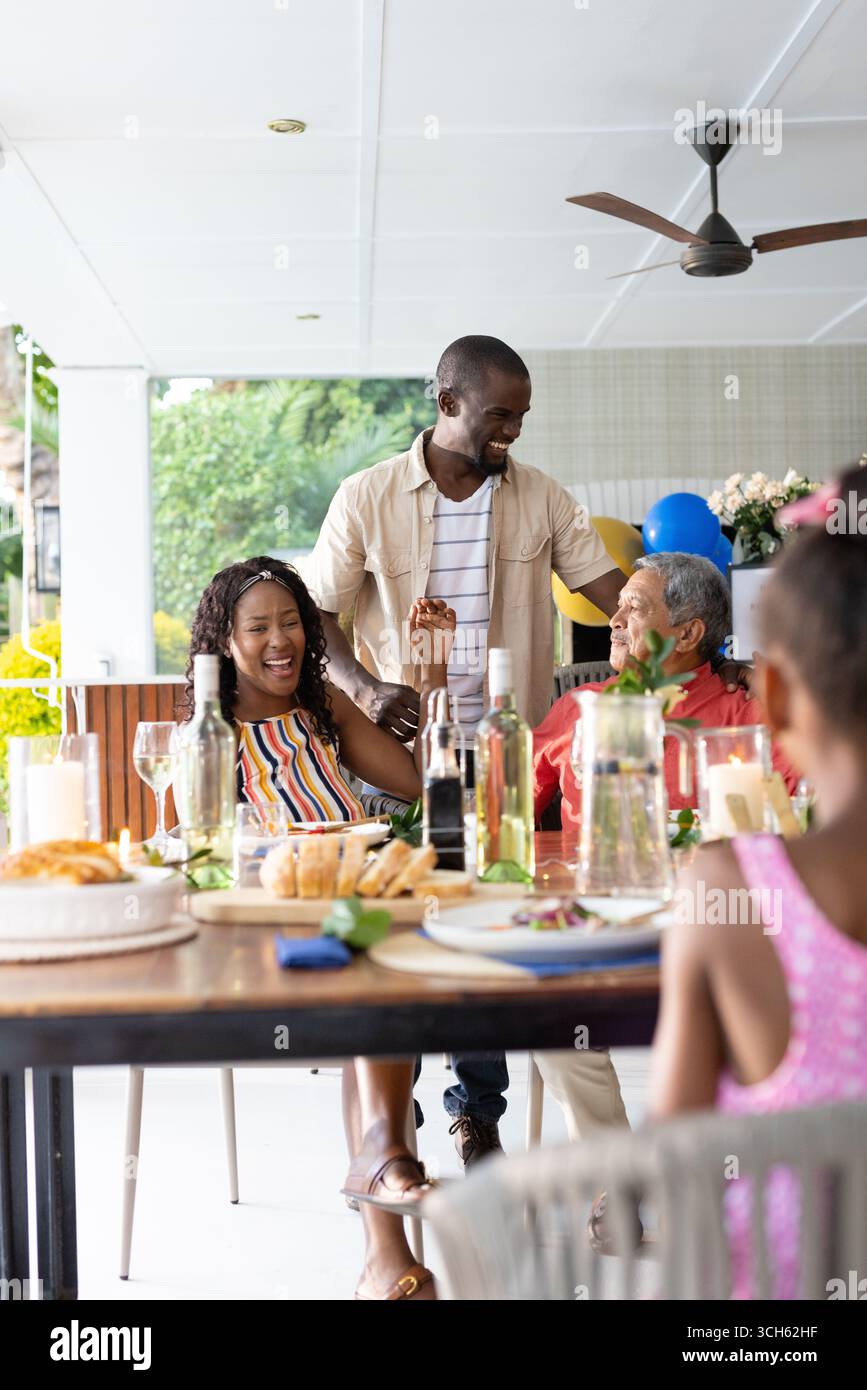 Sharing meal outdoors, African American family laughing and conversing ...