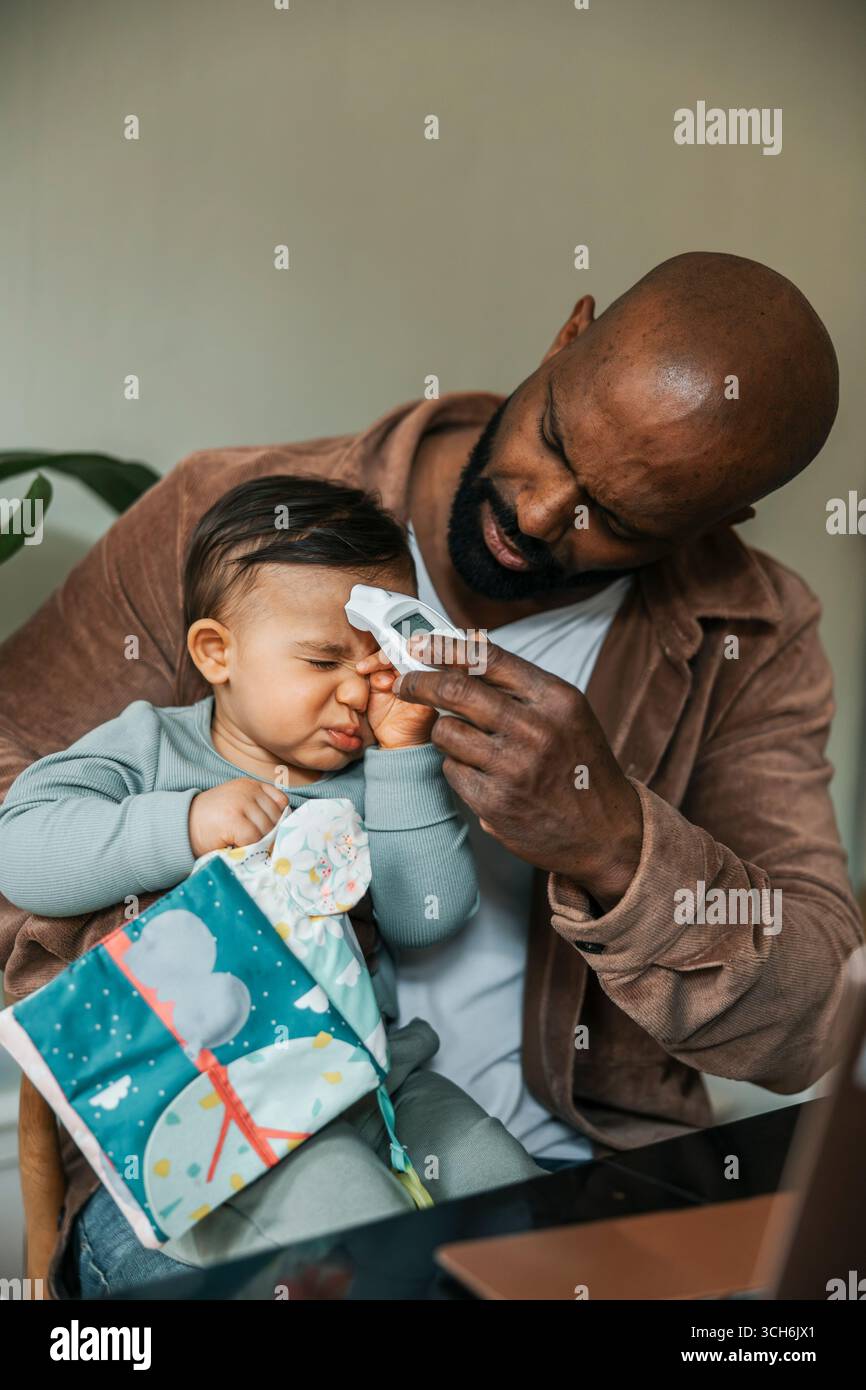 Father checking temperature of sick son with digital thermometer at ...