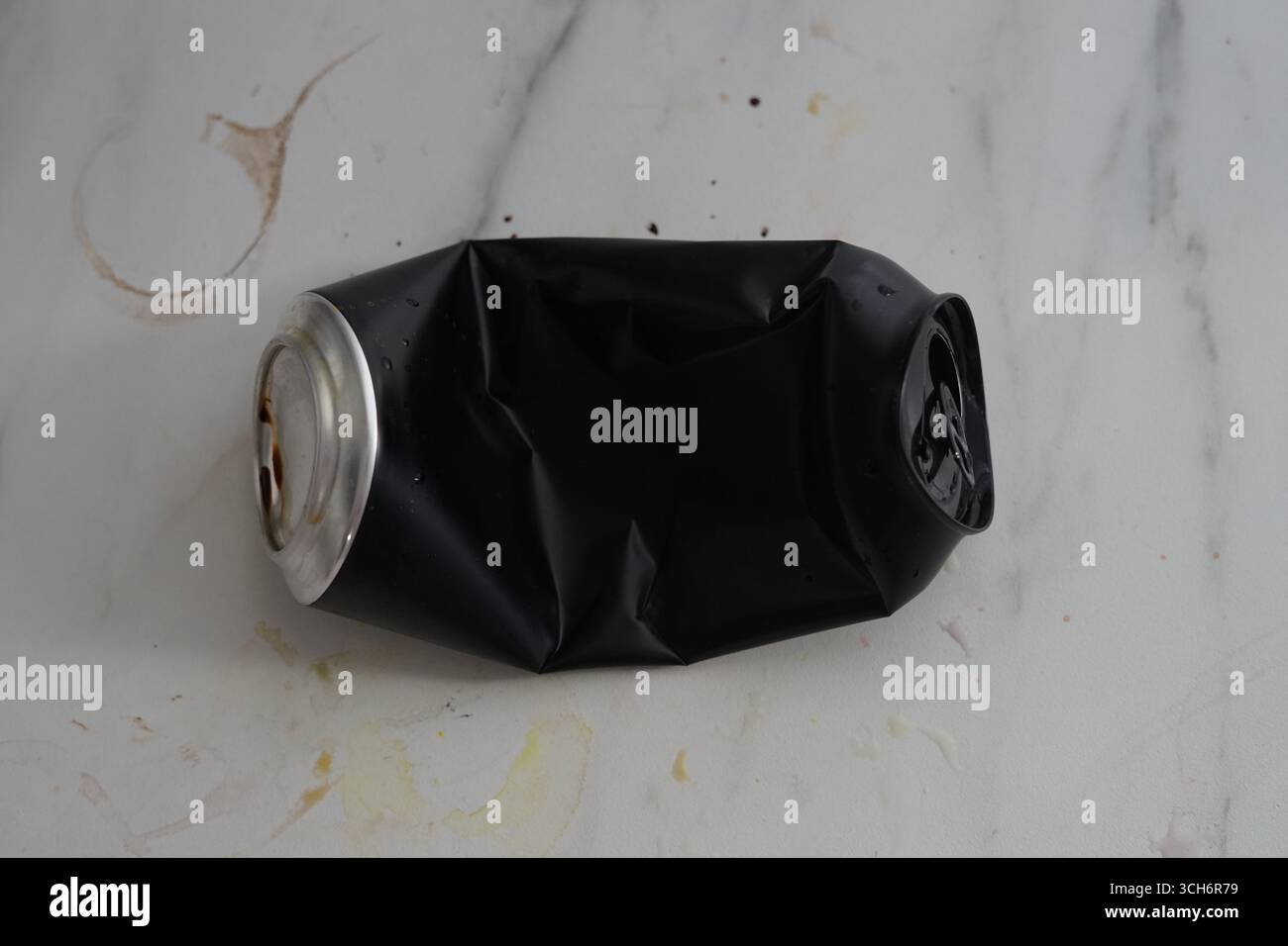 A crushed black beverage can resting on a marble surface, showcasing an ...