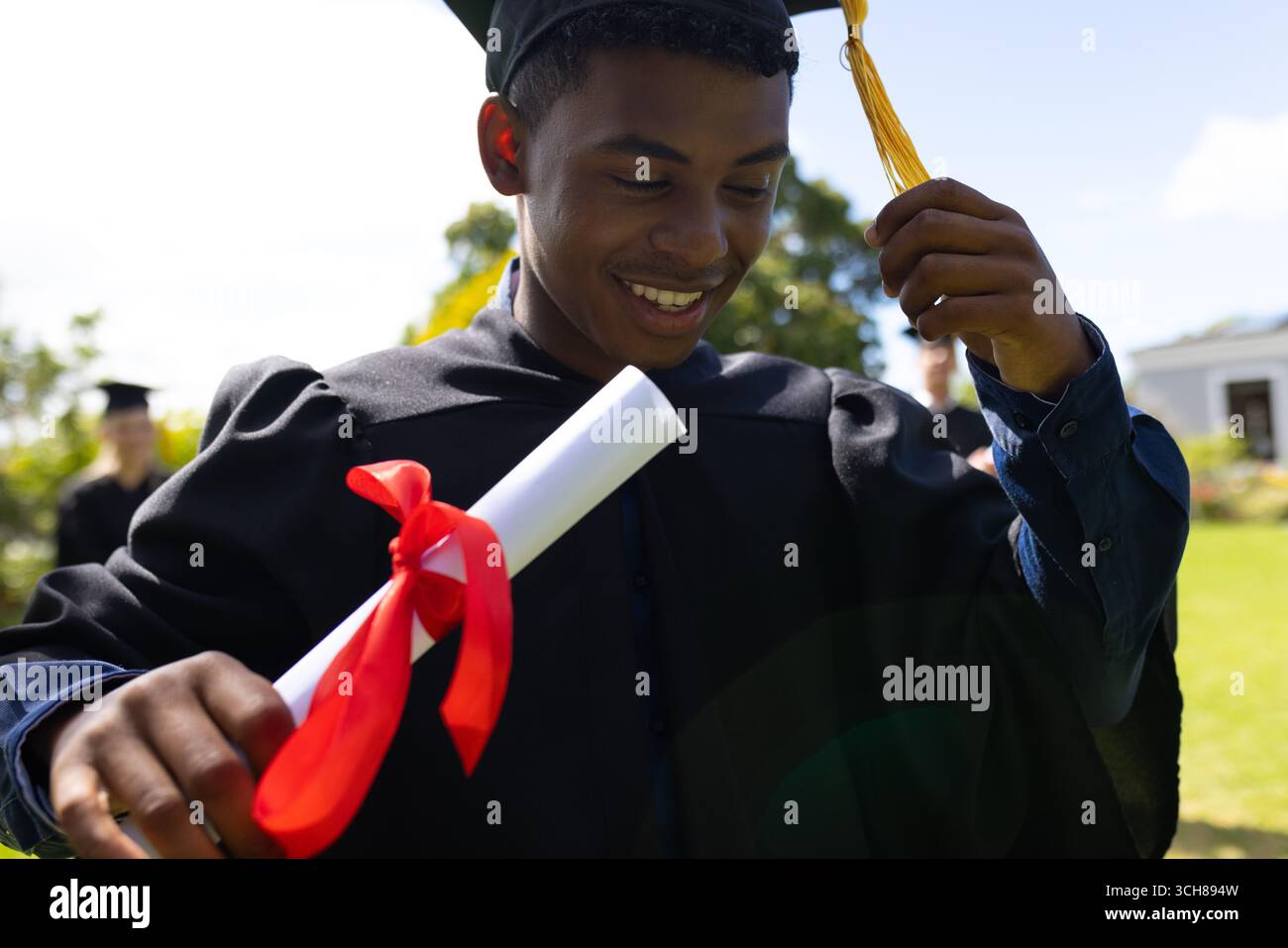 Teen graduate smiling outdoors, holding diploma with red ribbon ...