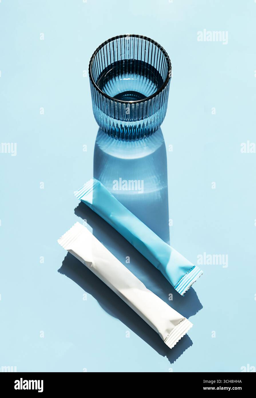 Two collagen supplement stick packs and glass of water on blue ...