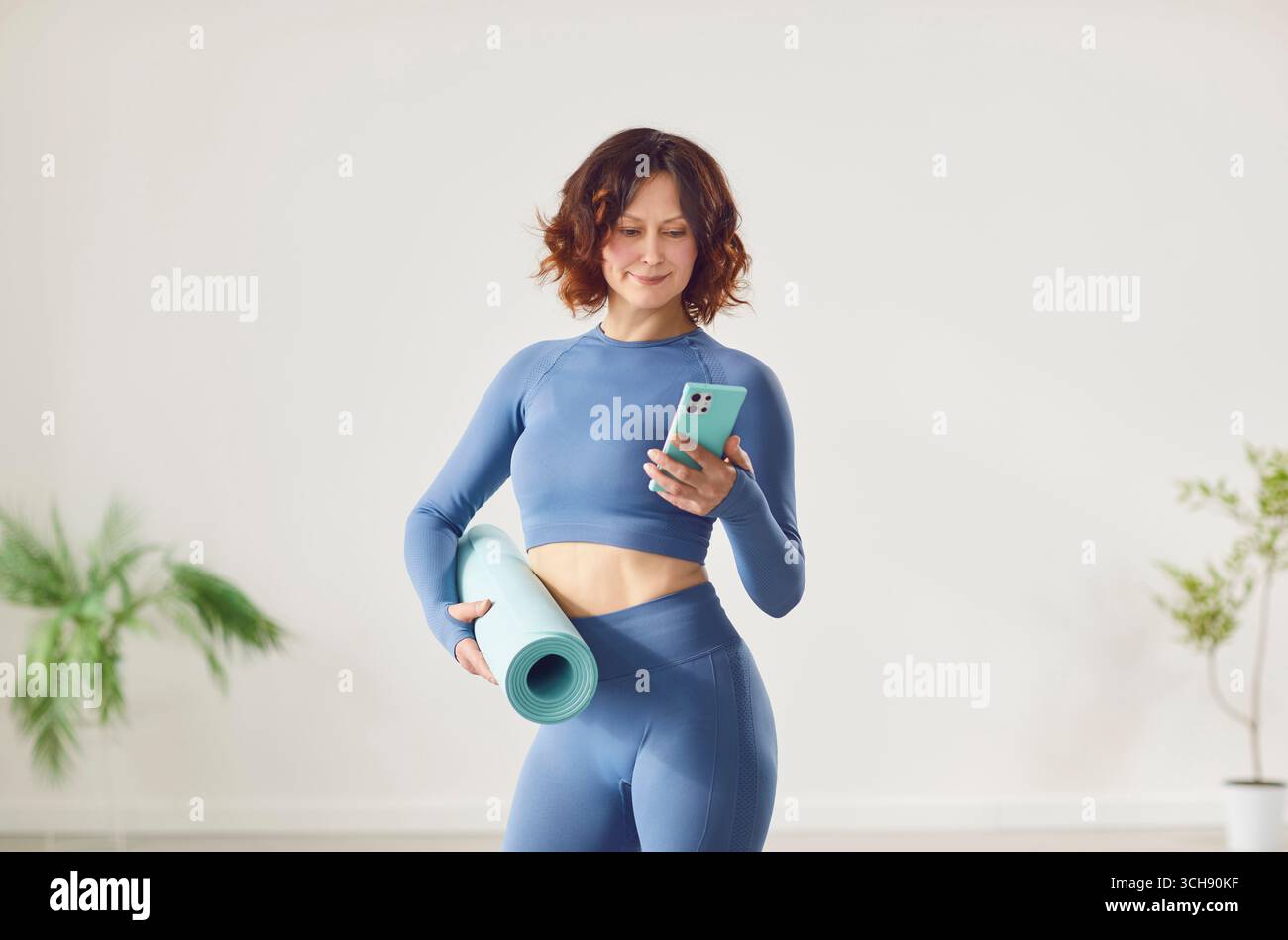 Sporty woman, yoga instructor standing holding mat checking mail ...