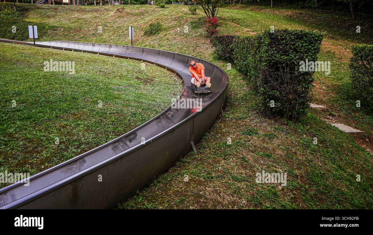 Man sliding down a metal summer toboggan run in a park, enjoying ...