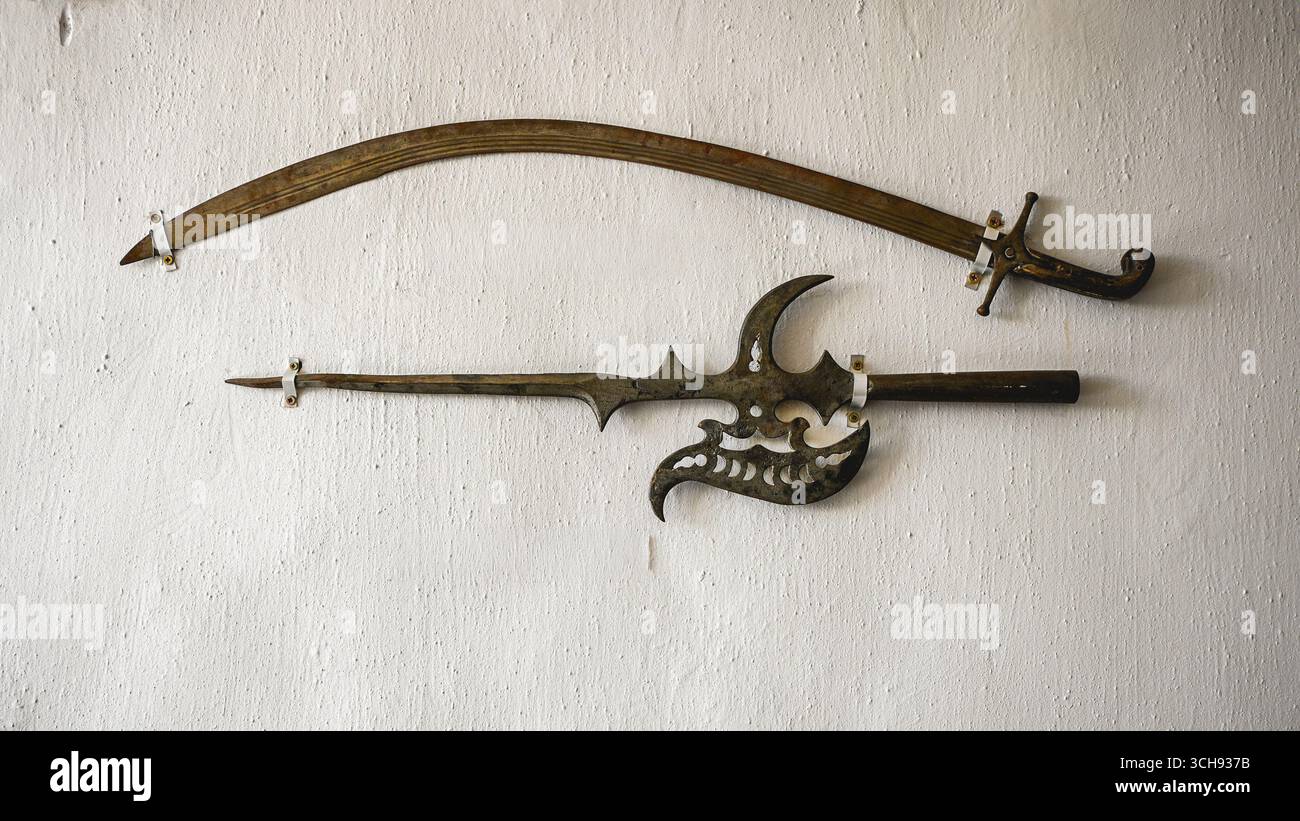 Two antique weapons, a scimitar and a halberd, are displayed on a white ...