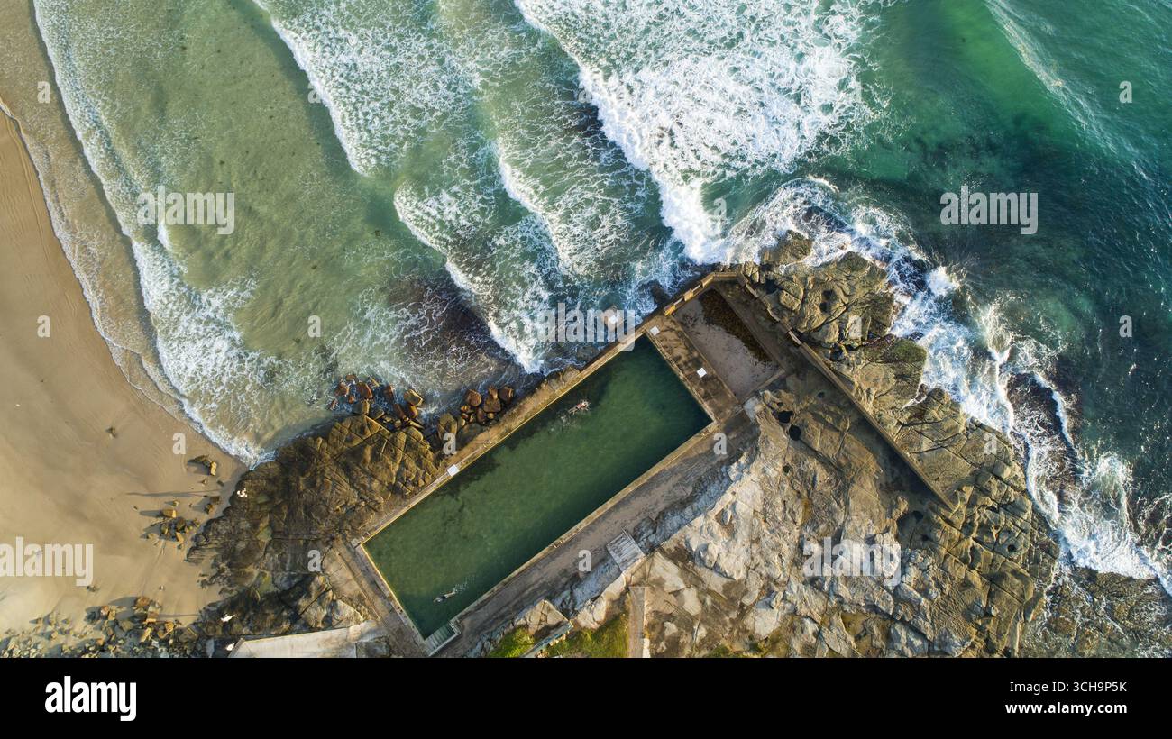 Aerial view of foamy waves crash against the rugged coastline ...