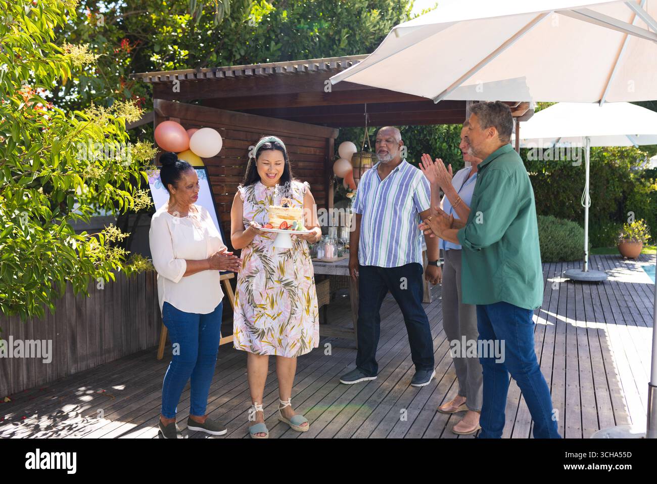 Celebrating outdoors, senior woman holding cake while diverse senior ...
